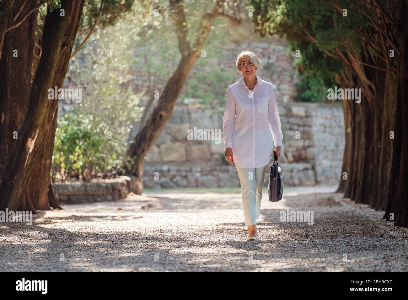 Business lady in eyeglasses walking in the park. Mature woman holding ...