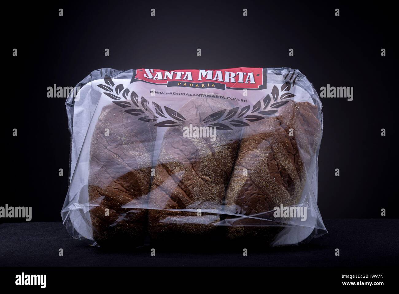 Fresh cereal bread in plastic wrap on white foam . Studio low key still ...