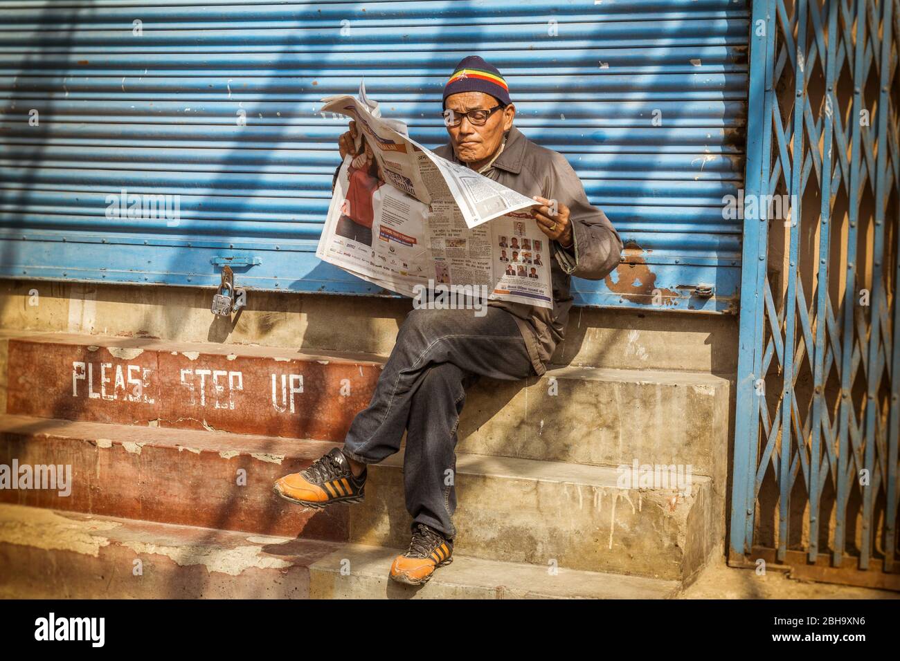 Elderly man sits on a staircase at the roadside and reads newspaper ...