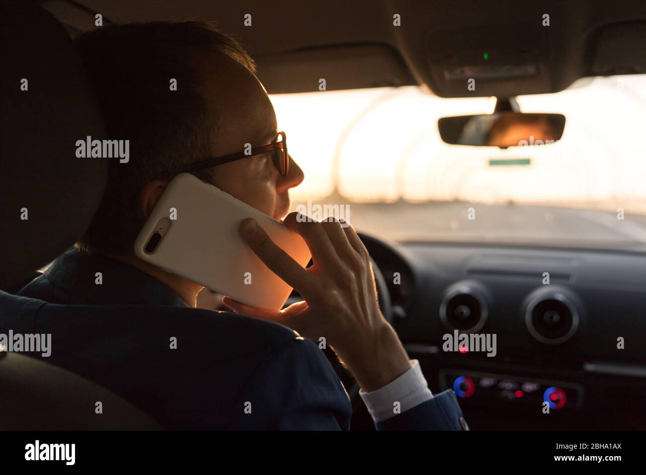 Man in blazer using and talking on smartphone while driving a car at ...