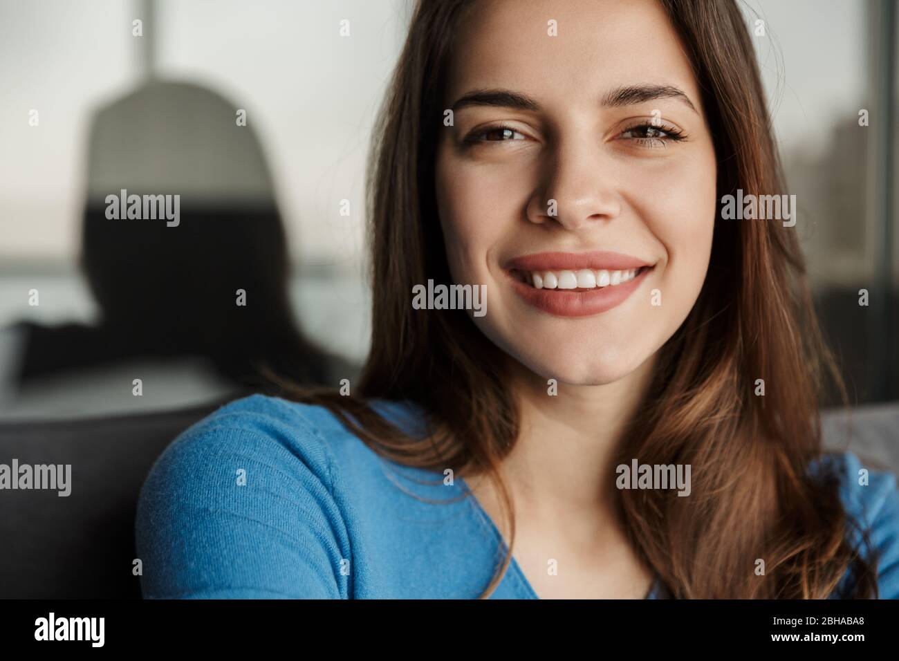 Image of young joyful woman looking at camera and smiling while sitting ...