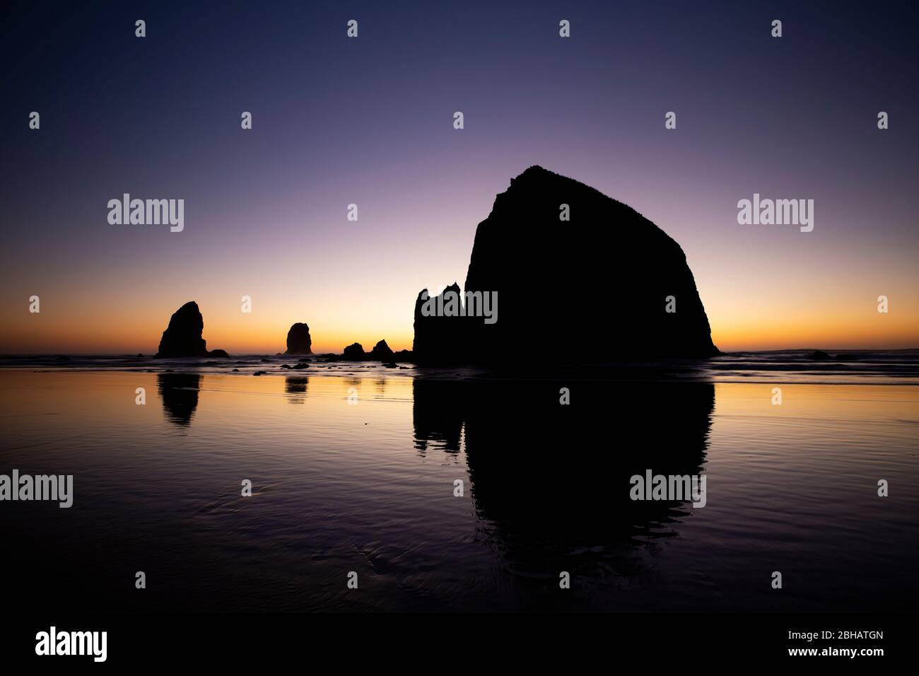 Rock formations reflecting in water at sunset, Cannon Beach, Oregon ...