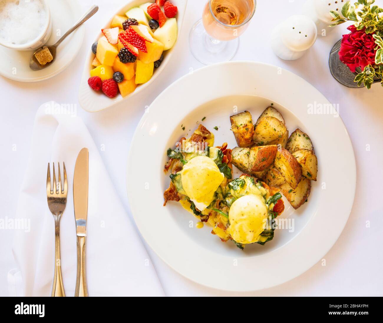 brunch of apple wood smoked bacon and eggs Benedict with fruit, a glass ...