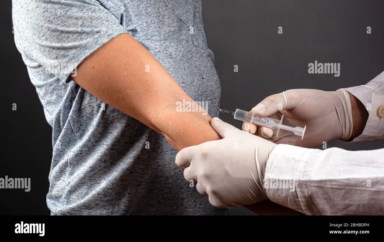doctor makes an injection in the patient’s arm on a dark background ...