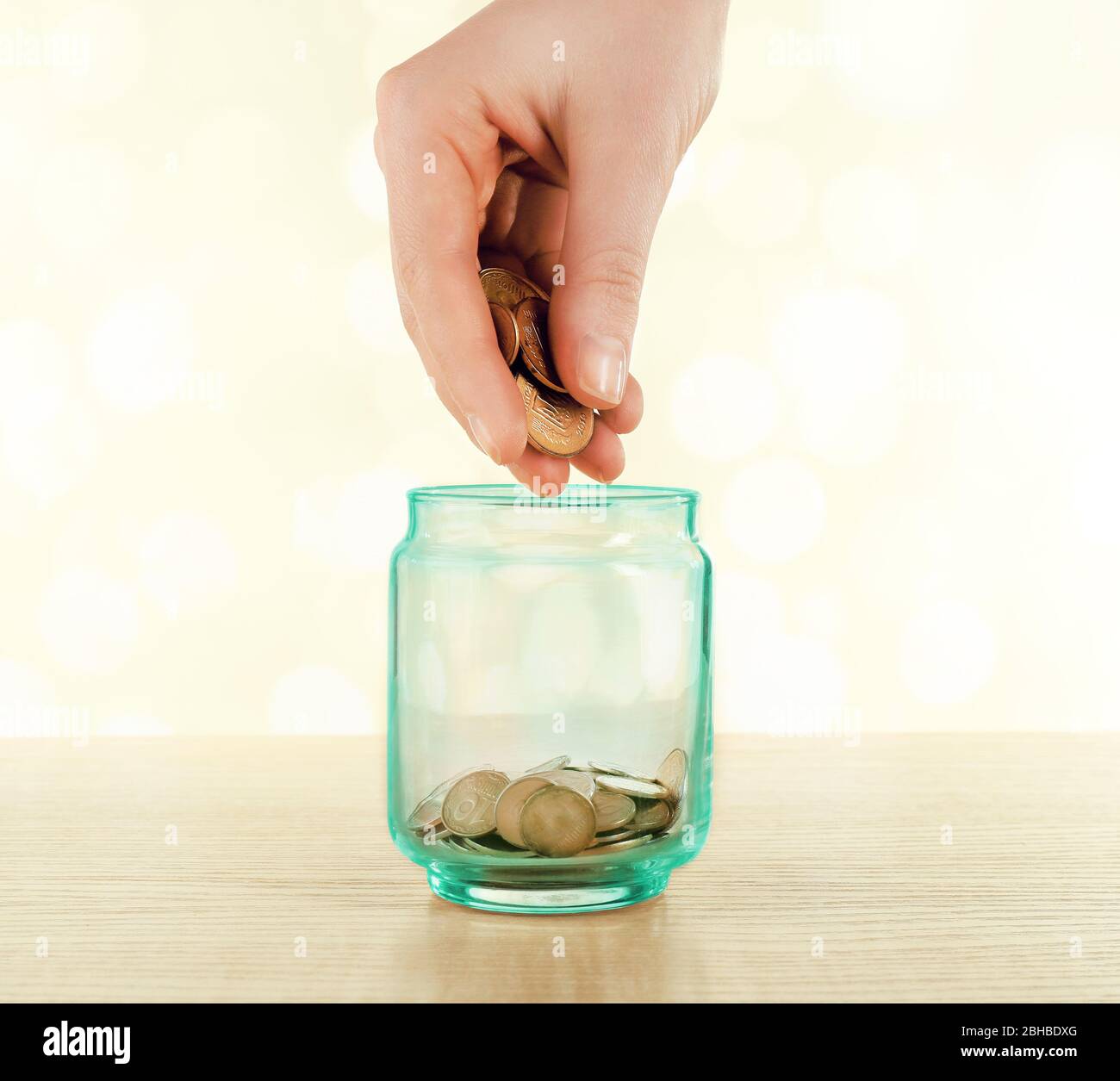 Female hand putting coins in glass bottle on bright blurred background ...