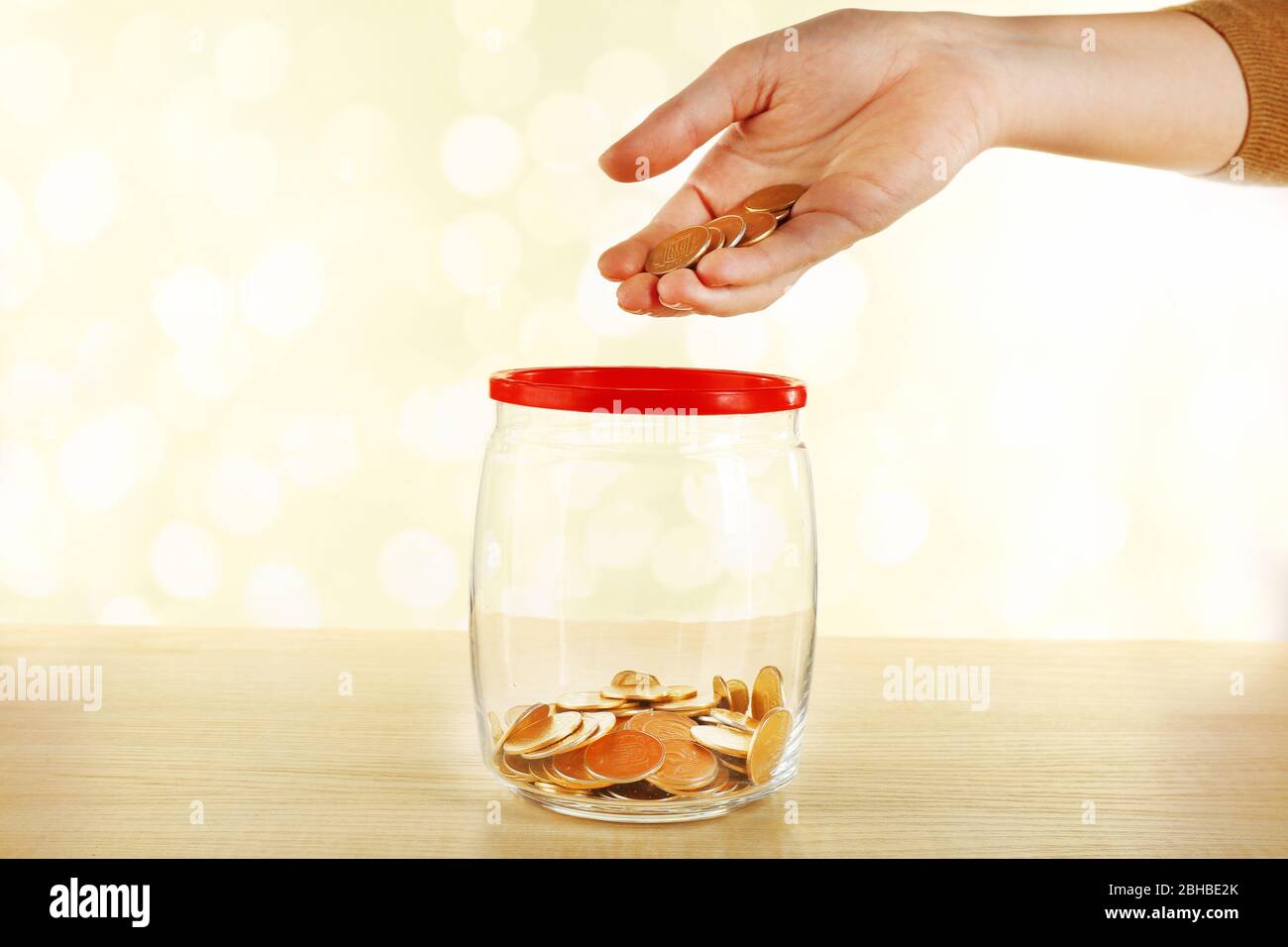 Female hand putting coins in glass bottle on bright blurred background ...