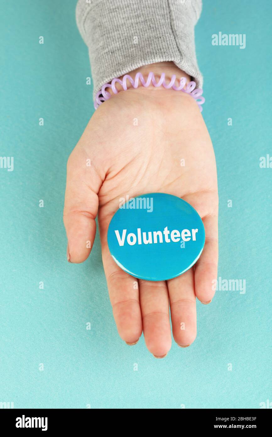 Round volunteer button in hand on colorful background Stock Photo - Alamy