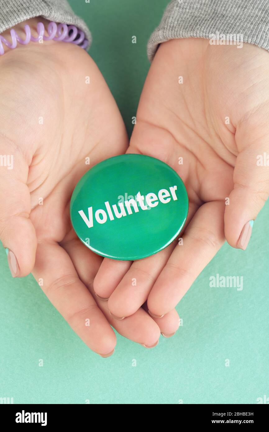 Round volunteer button in hands on colorful background Stock Photo - Alamy