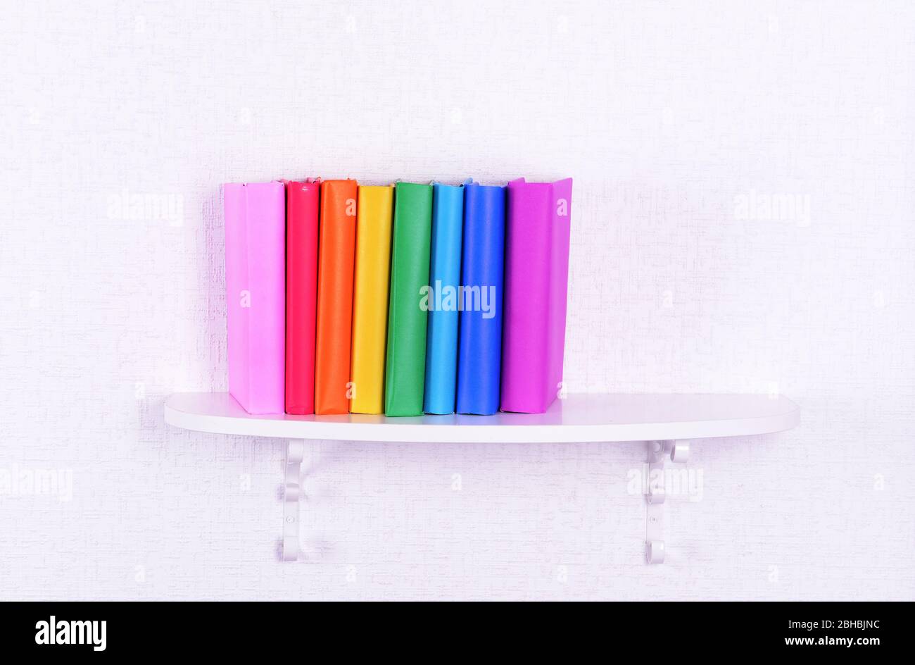Colorful books on shelf on white wall background Stock Photo - Alamy