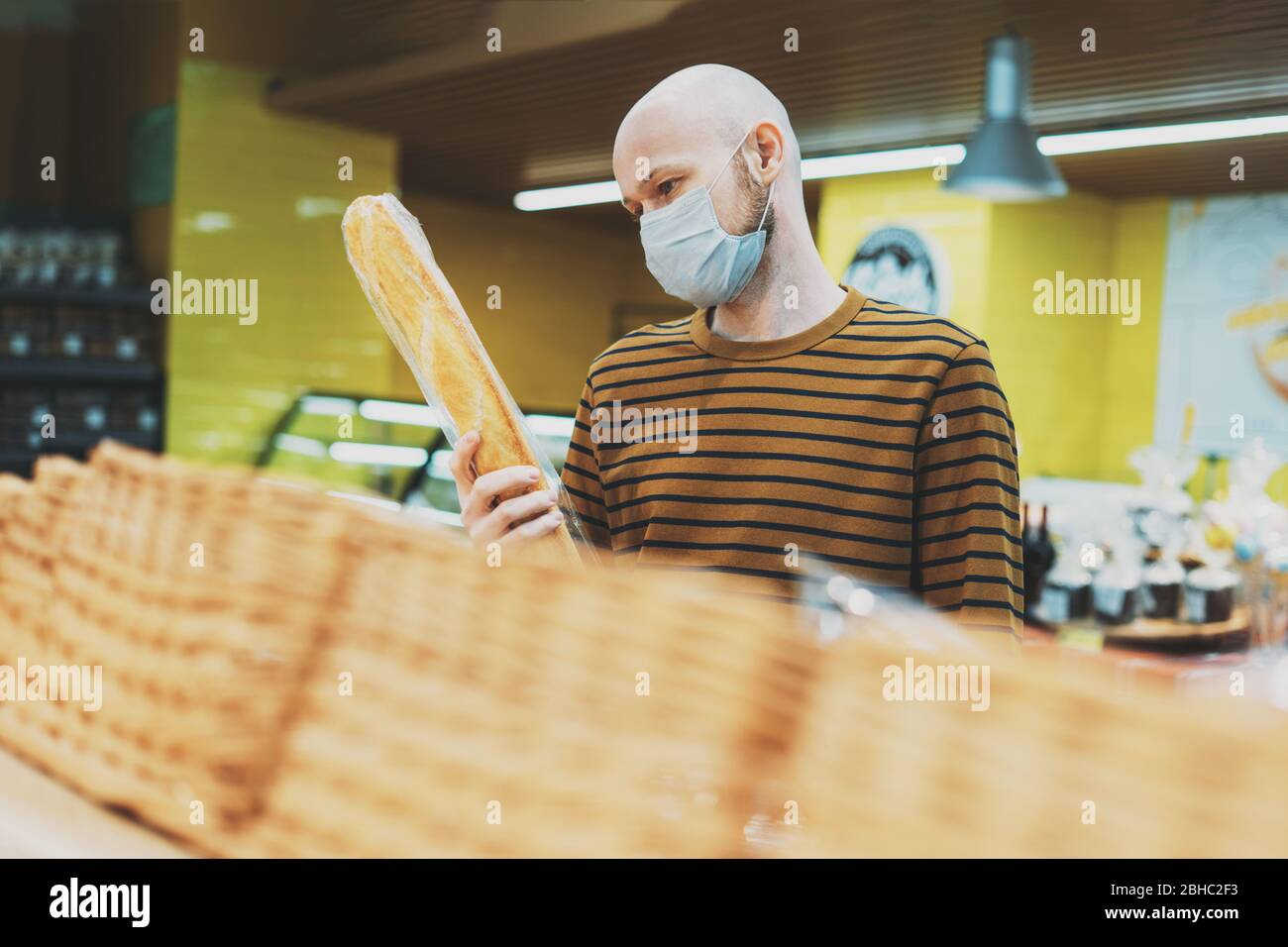 Adult bald man in medical face mask chooses bread in supermarket ...