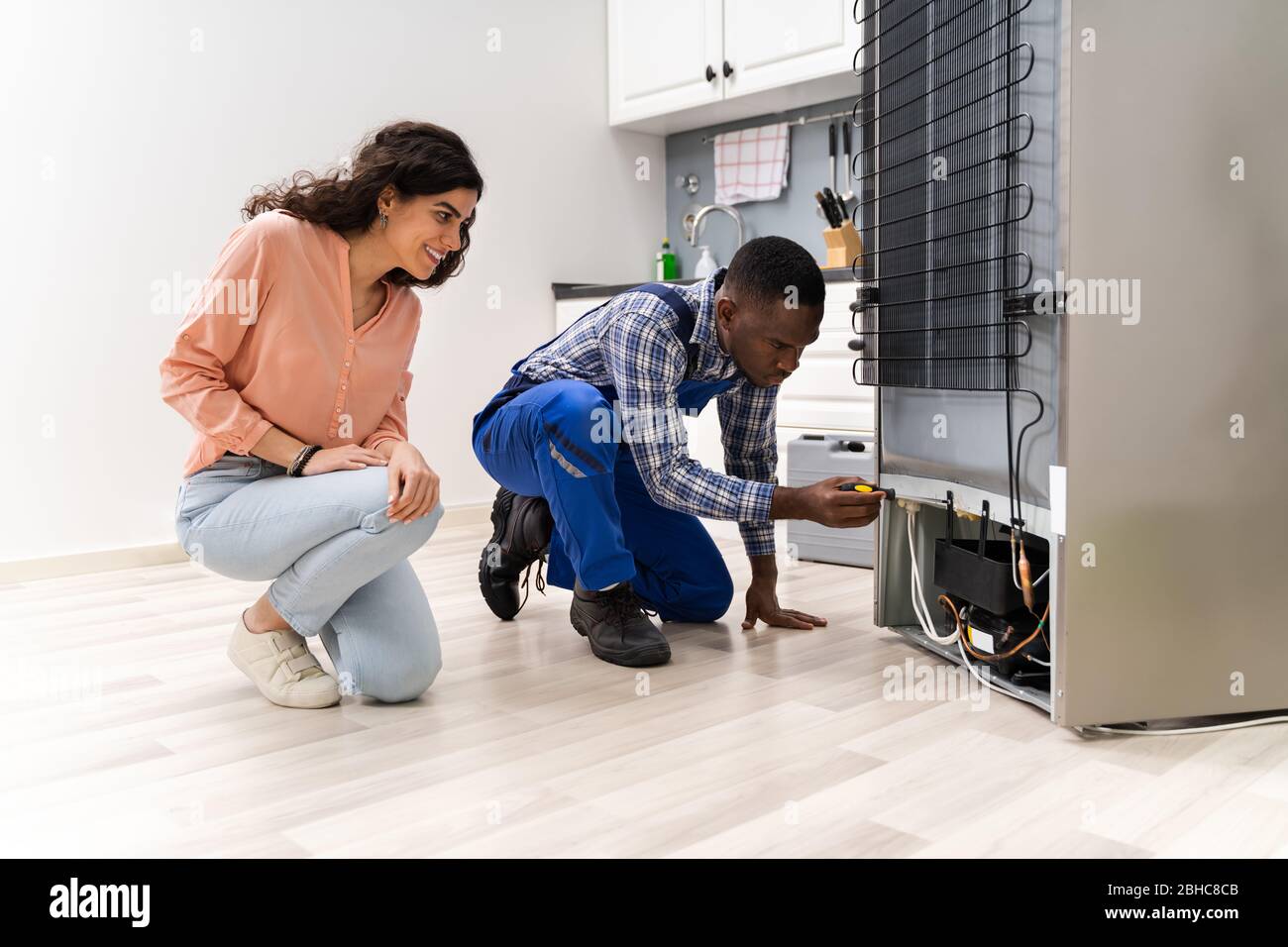 Young Repairman Repairing Refrigerator In Front Of Beautiful Woman ...