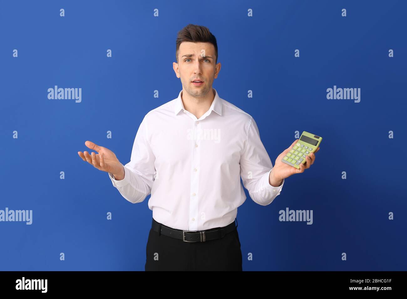 Confused young man with calculator on color background Stock Photo - Alamy