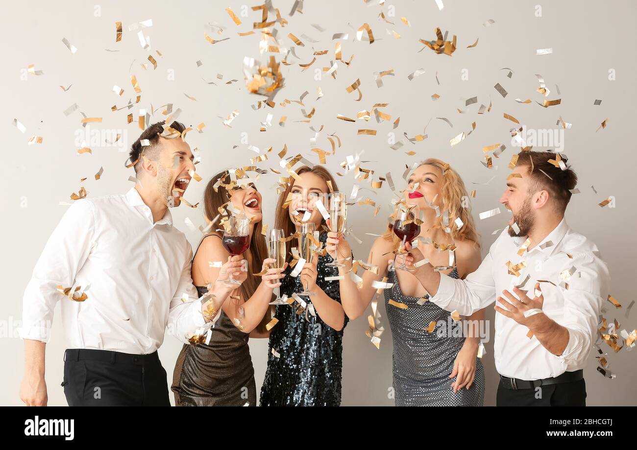 Happy people with glasses of alcoholic drinks and confetti on grey ...
