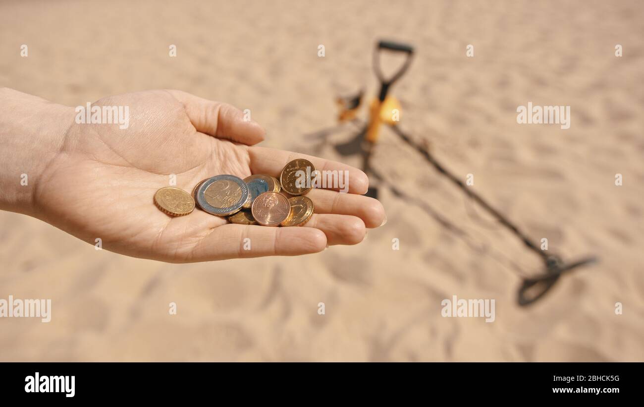 Close up, hands with the coins. Person searching sandy beach with metal ...