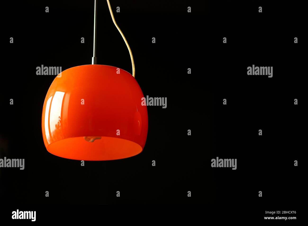 Black background with a warm orange hanging lamp and negative space ...