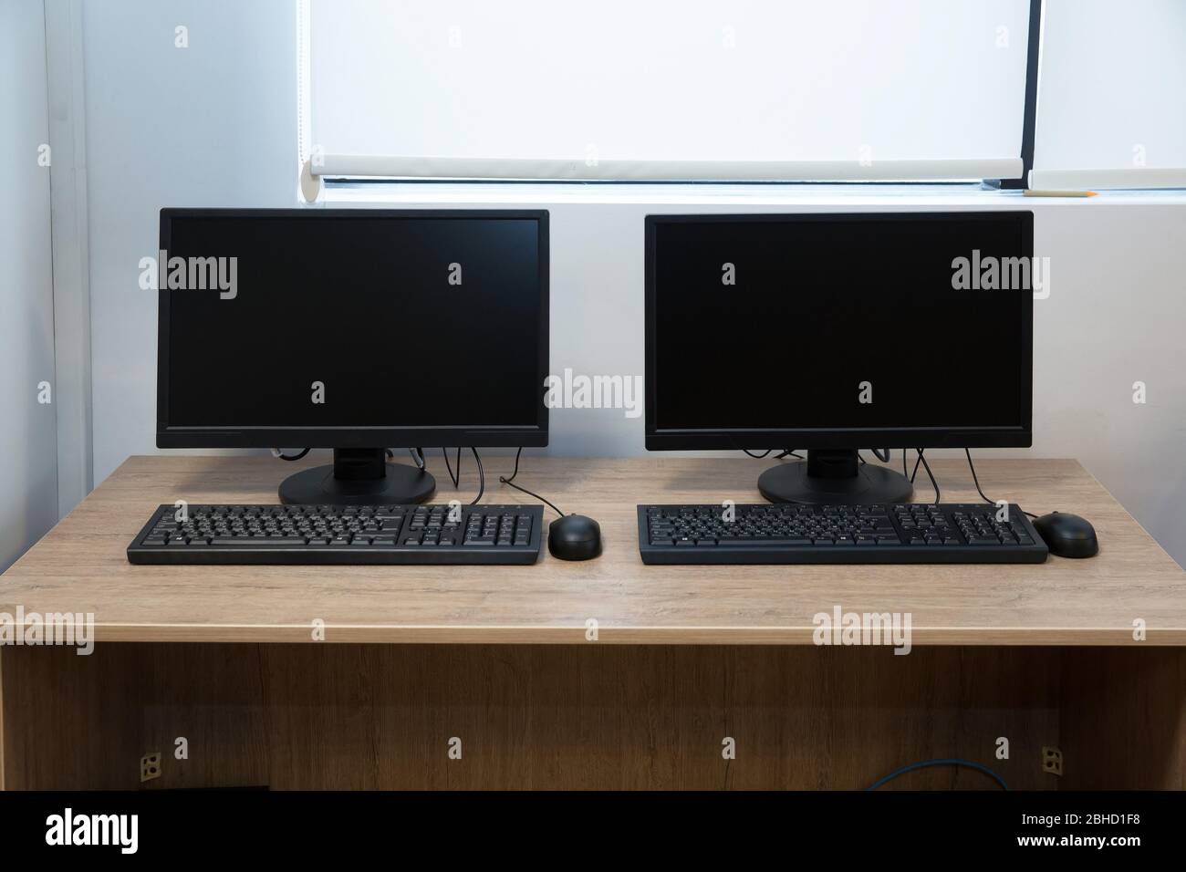 two computers and a desk . Keyboard and mouse . Two computer monitors with a black screen on a ...