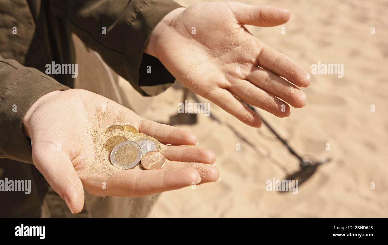 Close up, hands with the coins. Person searching sandy beach with metal ...
