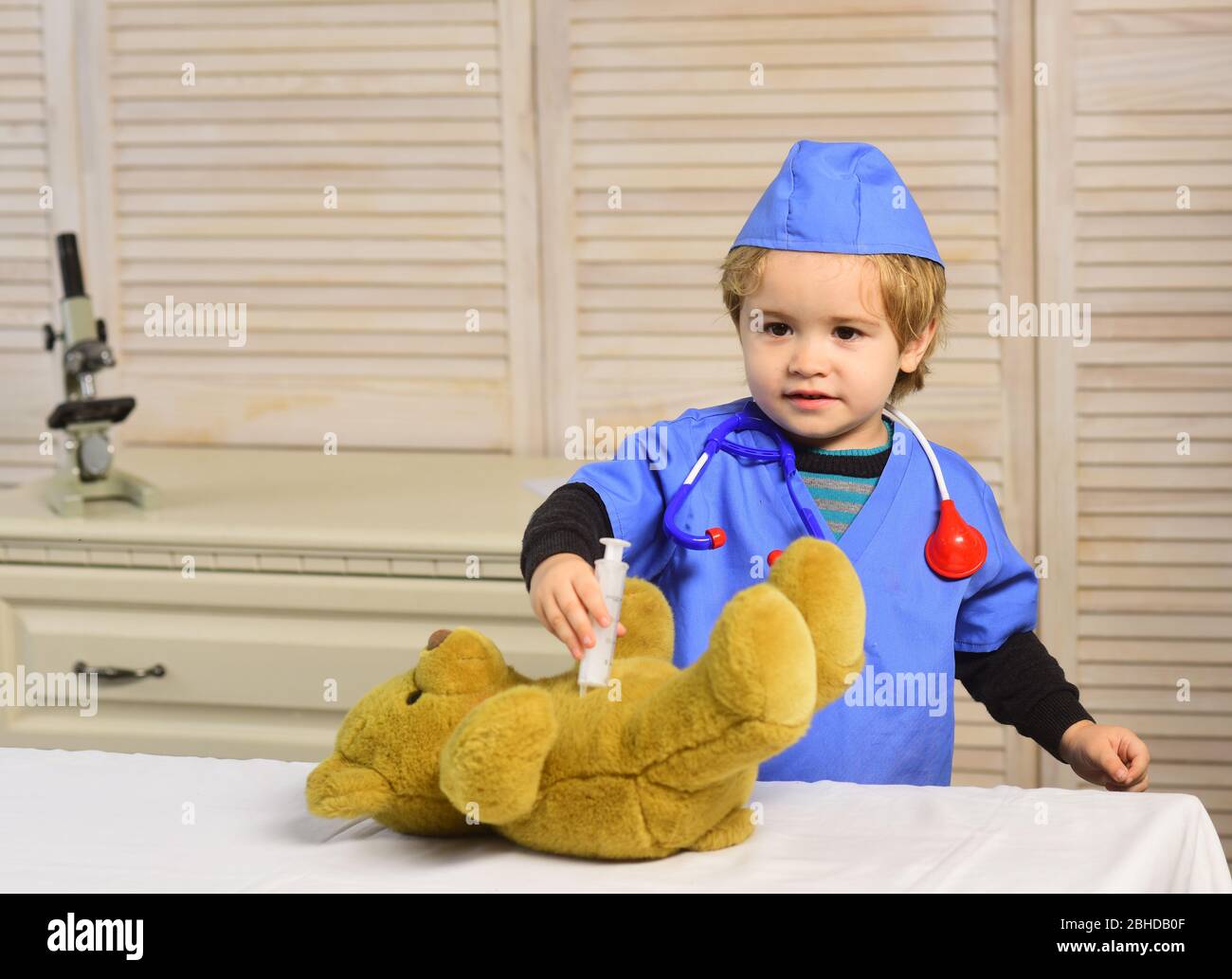 Boy in surgical uniform holds syringe on wooden background. Healthcare ...