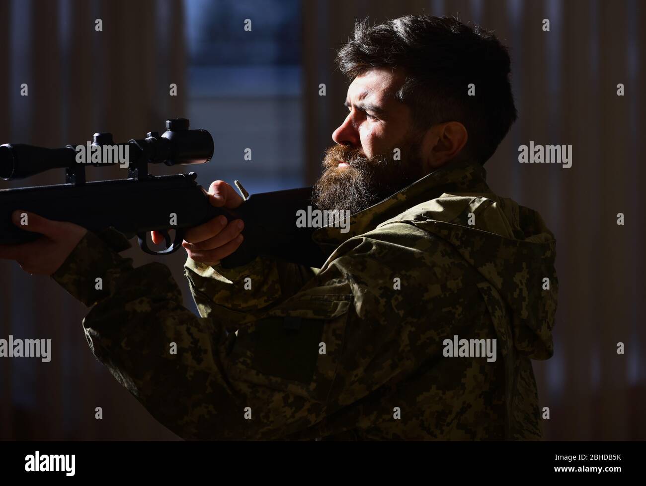 Man with beard wears camouflage clothing, dark interior background ...