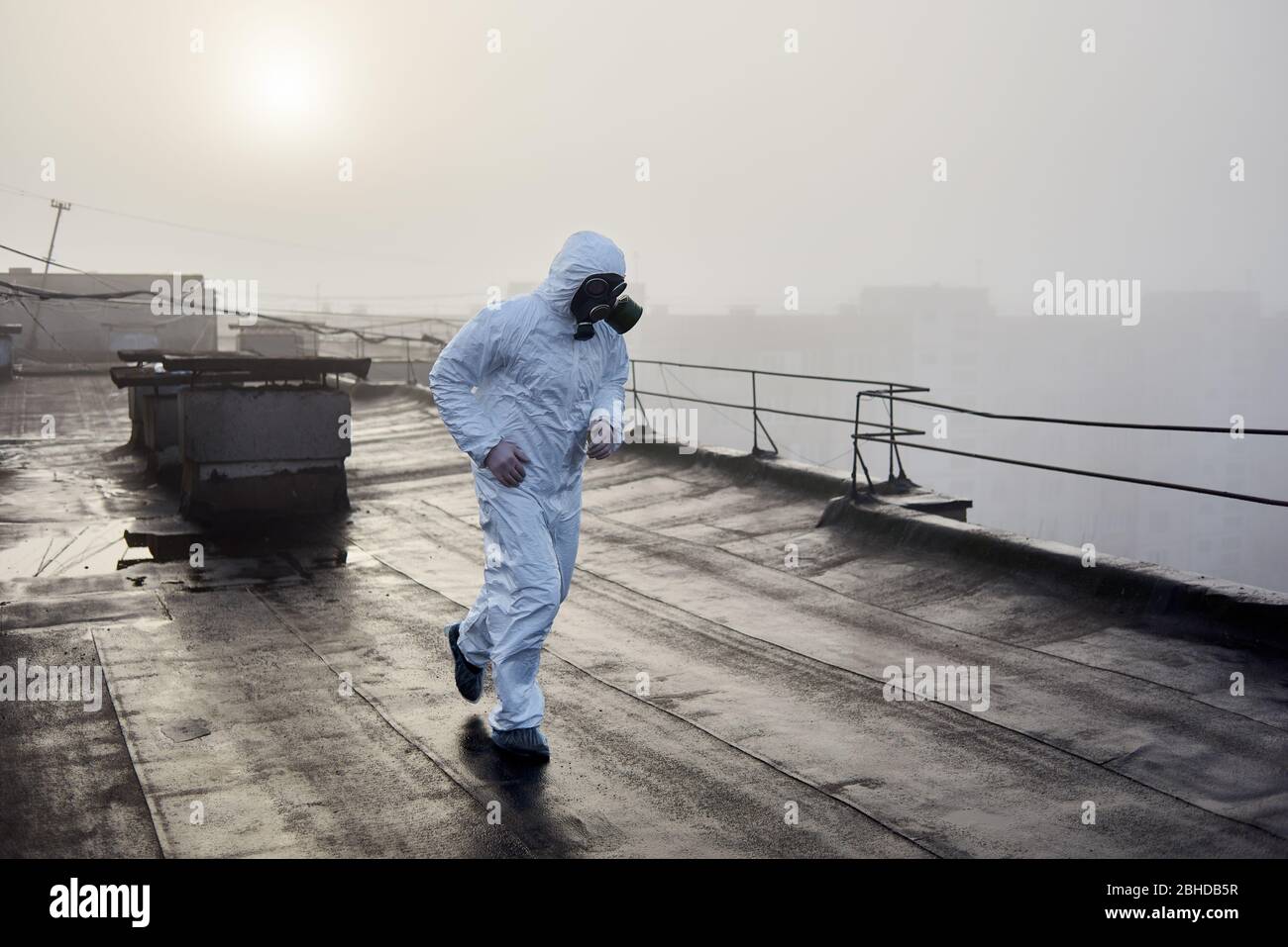Man wearing white coverall and gas mask, running on the roof of an ...