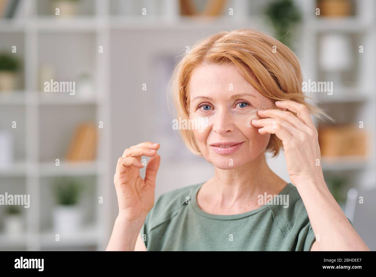 Mature female with blond hair putting under eye patches on her face ...