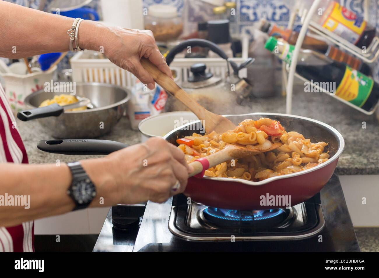 Old woman cooking macaroni pasta in flying pan in the kitchen Stock ...