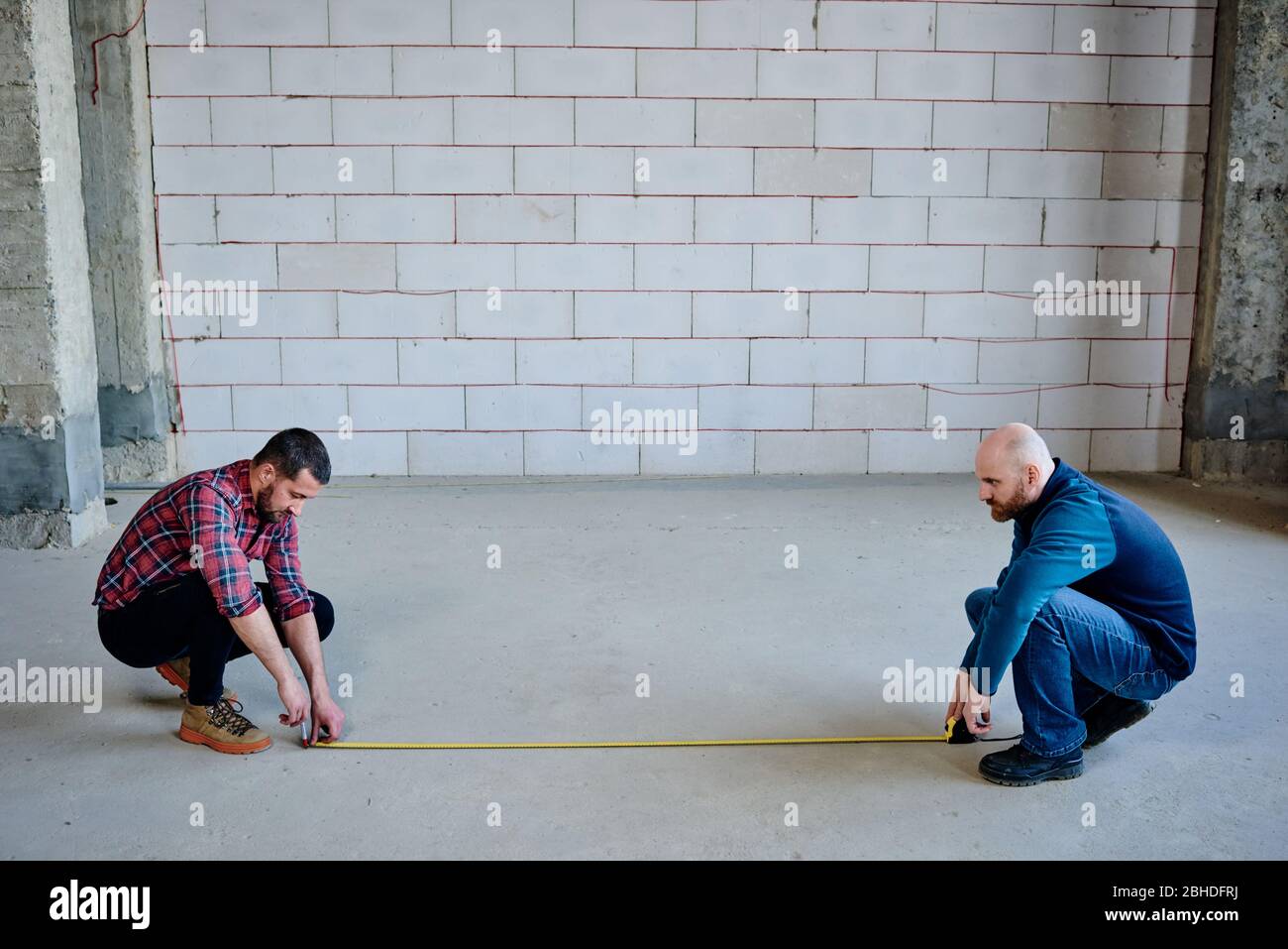 Two young engineers sitting on squats and measuring width of aperture ...