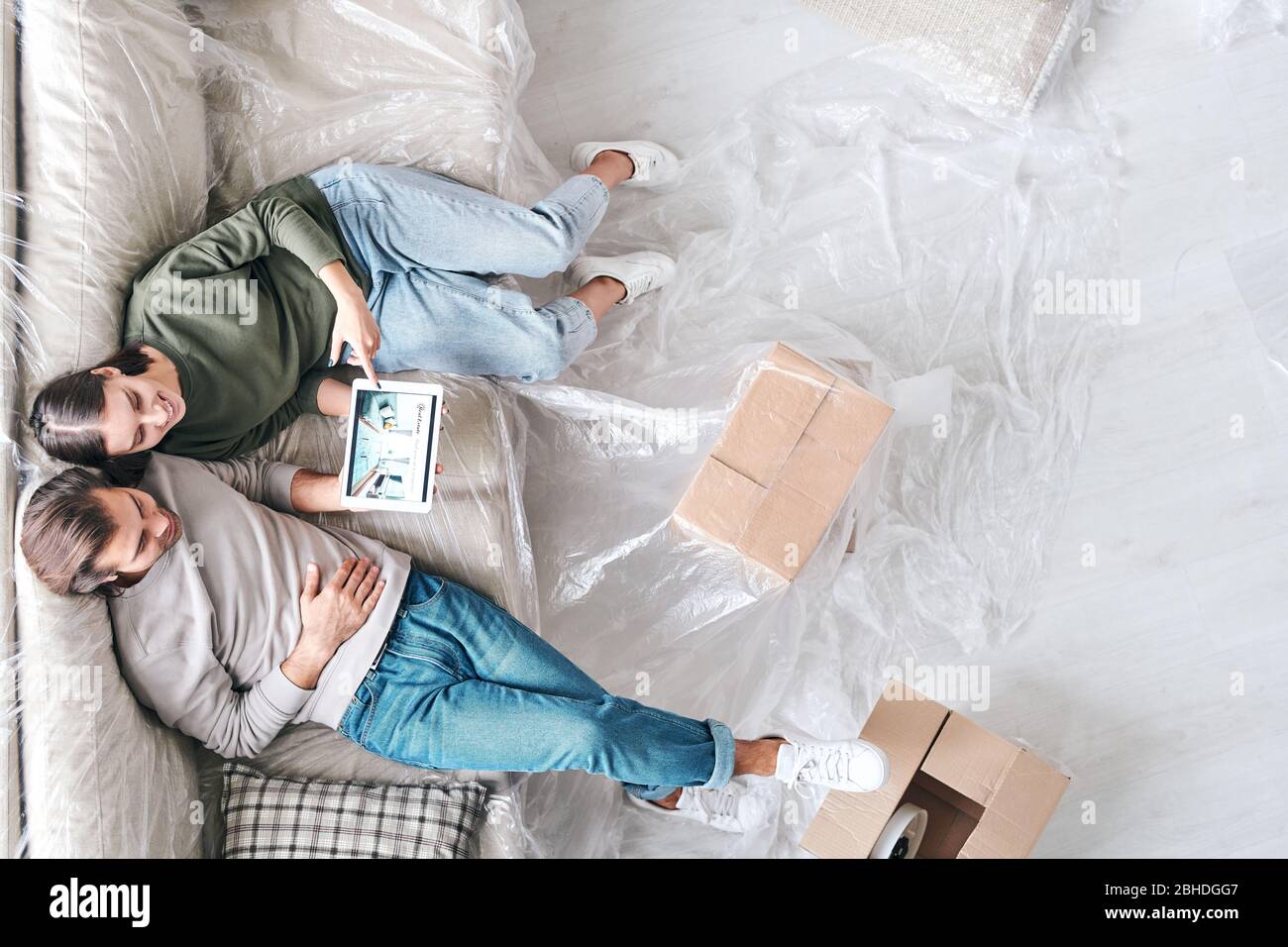 Overview of young affectionate couple with tablet sitting on new couch ...