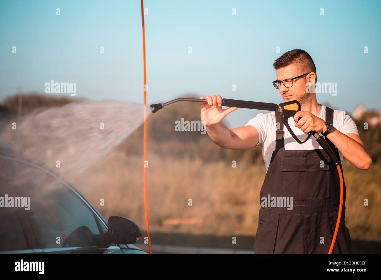 Young man washing car outdoors in a car wash station using high ...