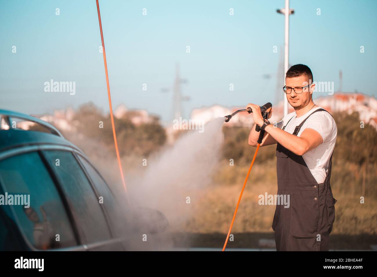 Male worker washing car outdoors in a car wash station using high ...