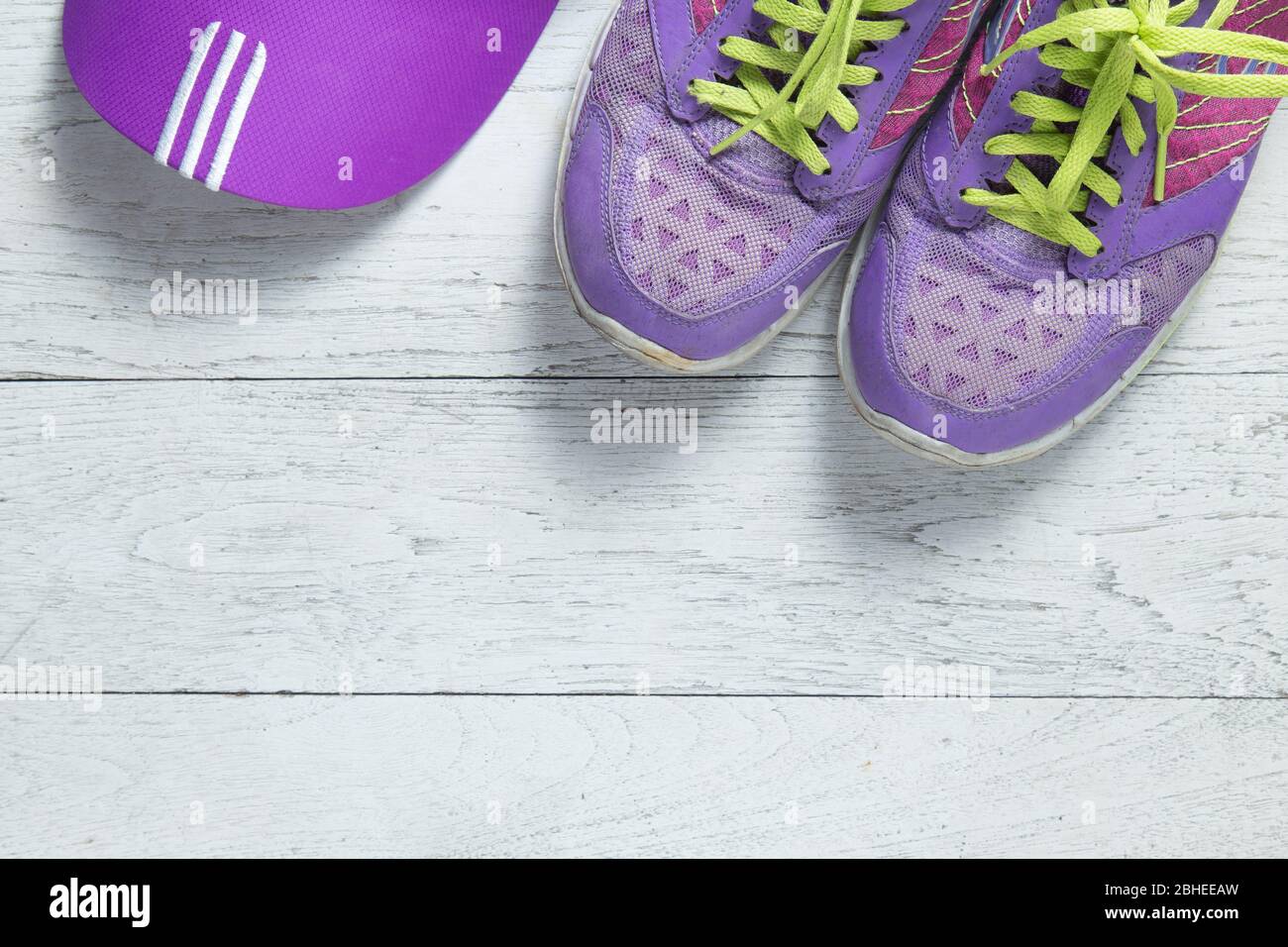 Sport flat lay purple shoes and cap on white wooden background with ...