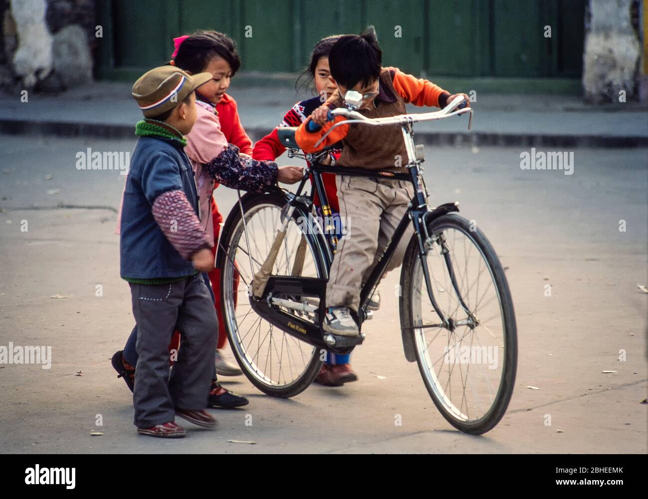 Yangshuo, China - Mar 1987: Children playing with a bicycle on a street ...