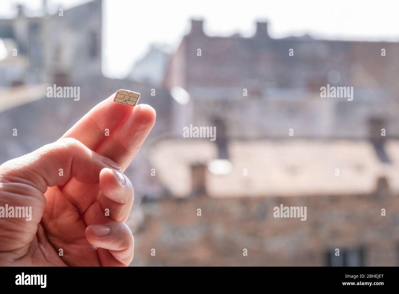 Hand holds a SIM Card on the street background with sky and houses ...