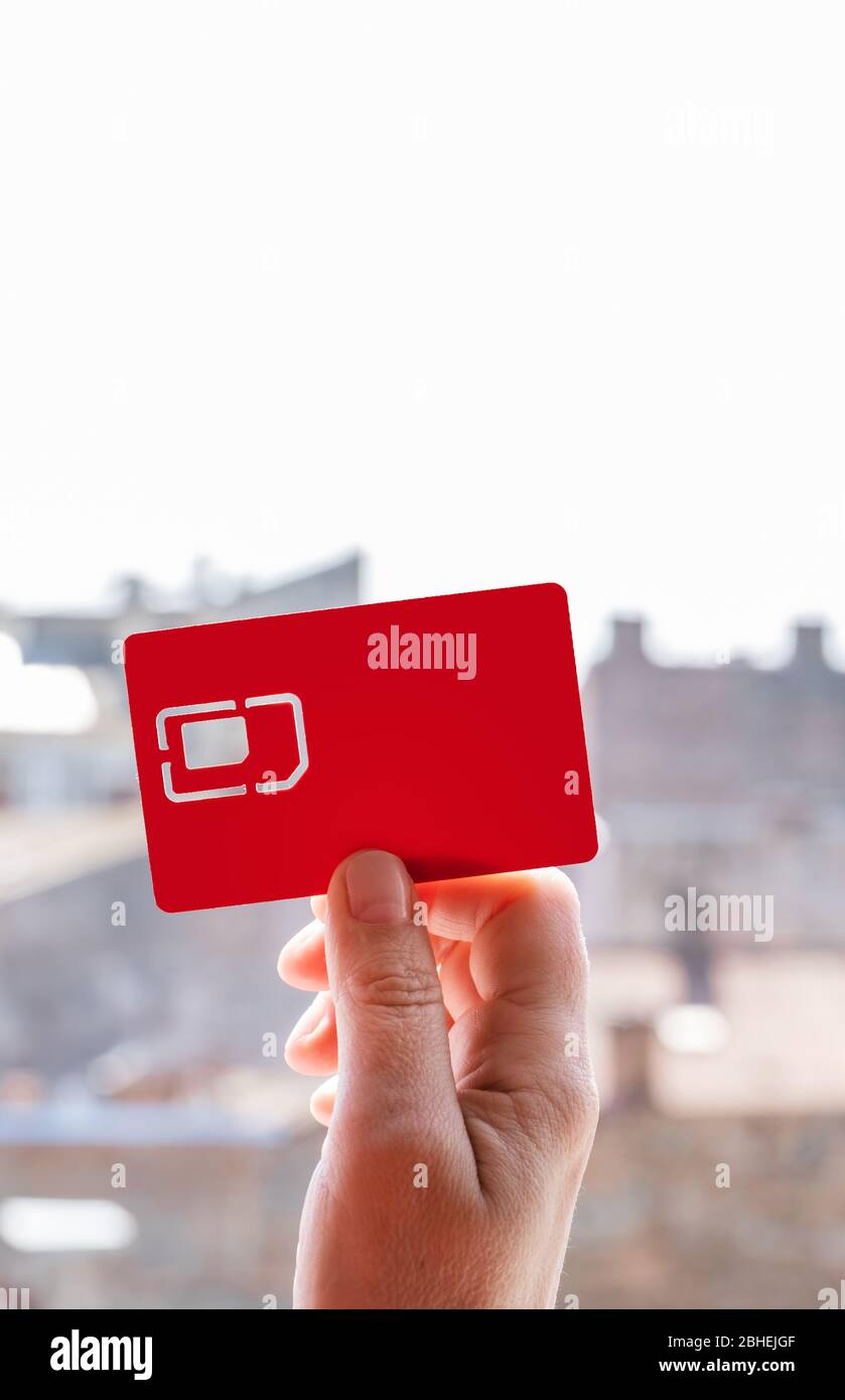 Hand holds a red SIM Card's slot on the street background with sky and ...