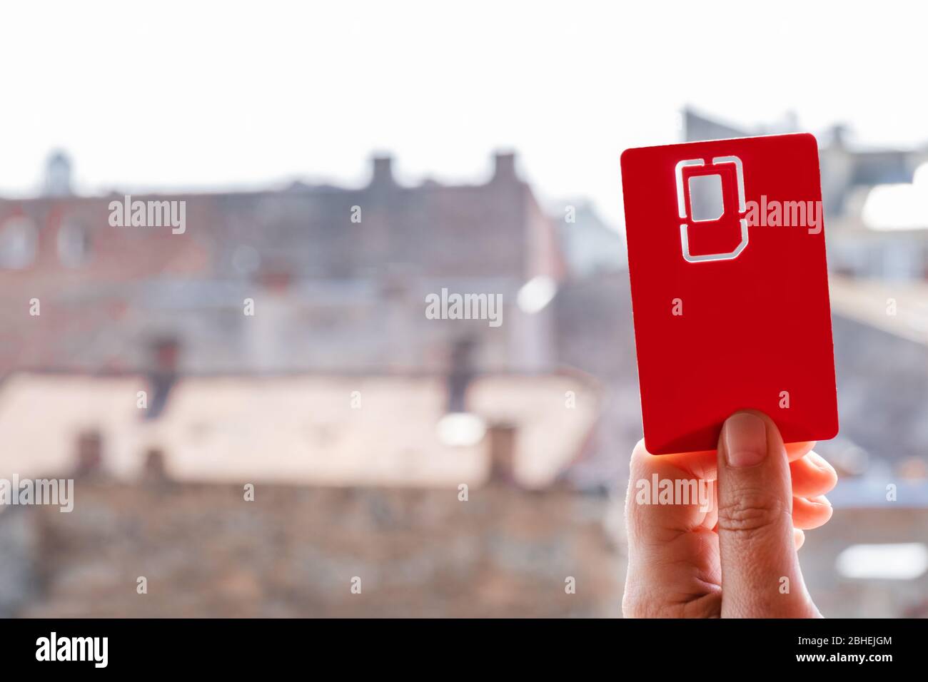 Hand holds a red SIM Card's slot on the street background with sky and ...