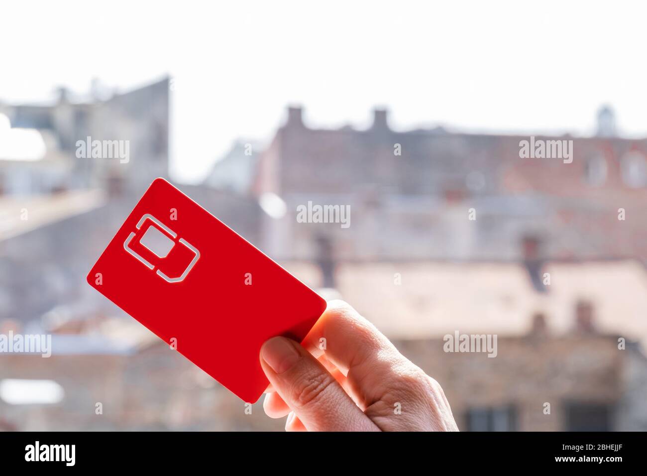 Hand holds a red SIM Card's slot on the street background with sky and ...