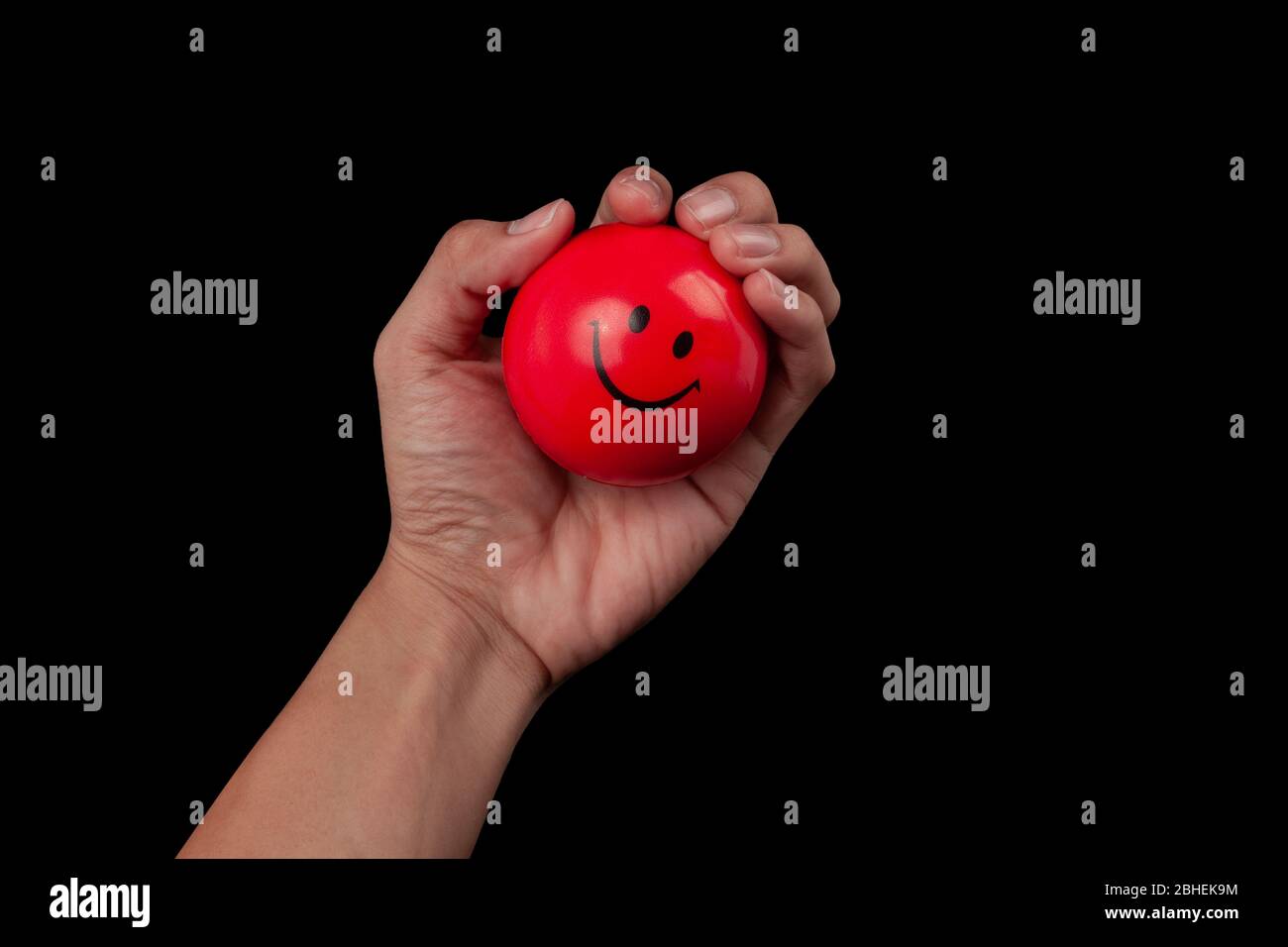 Hand squeezing a red stress ball isolated on black background with ...