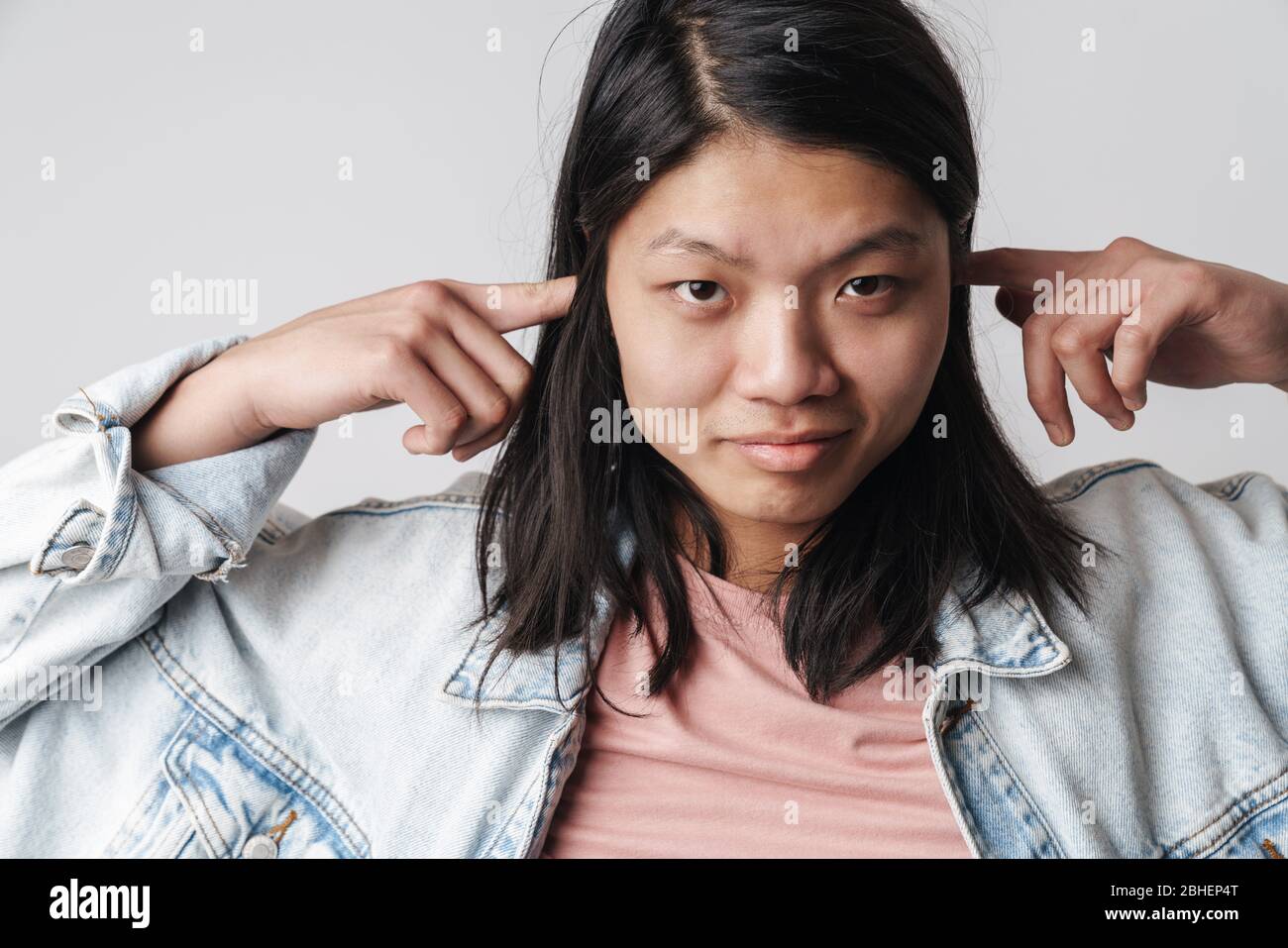 Image of pleased asian man looking at camera and plugging his ears ...