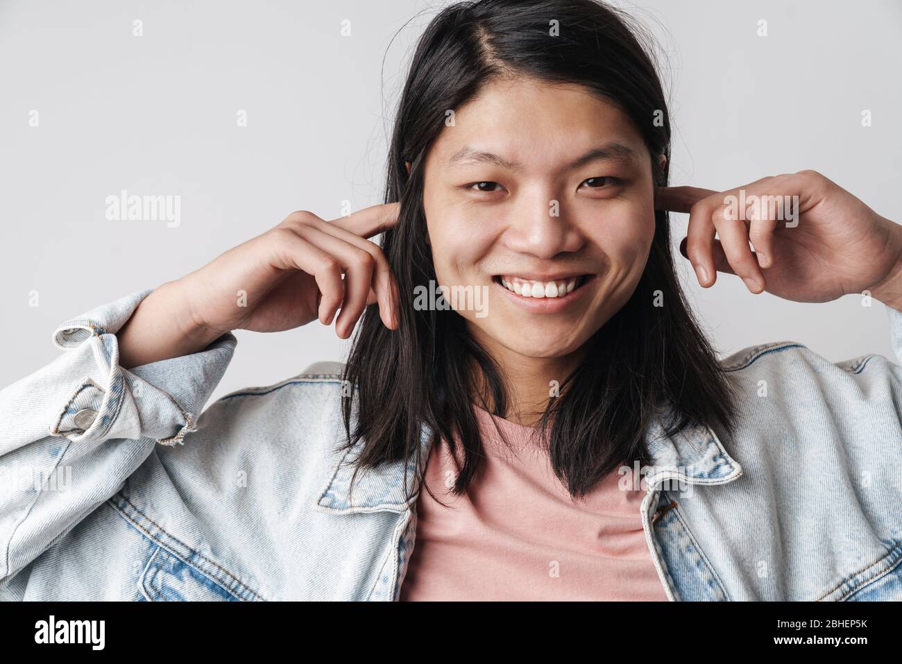 Image of pleased asian man smiling and plugging his ears isolated over ...