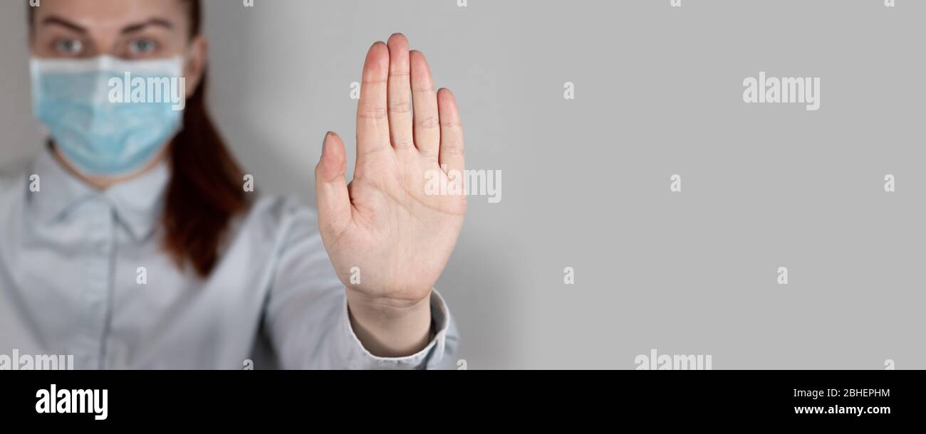 Paramedic in medical shows stop sign with hand on gray wall in clinic ...