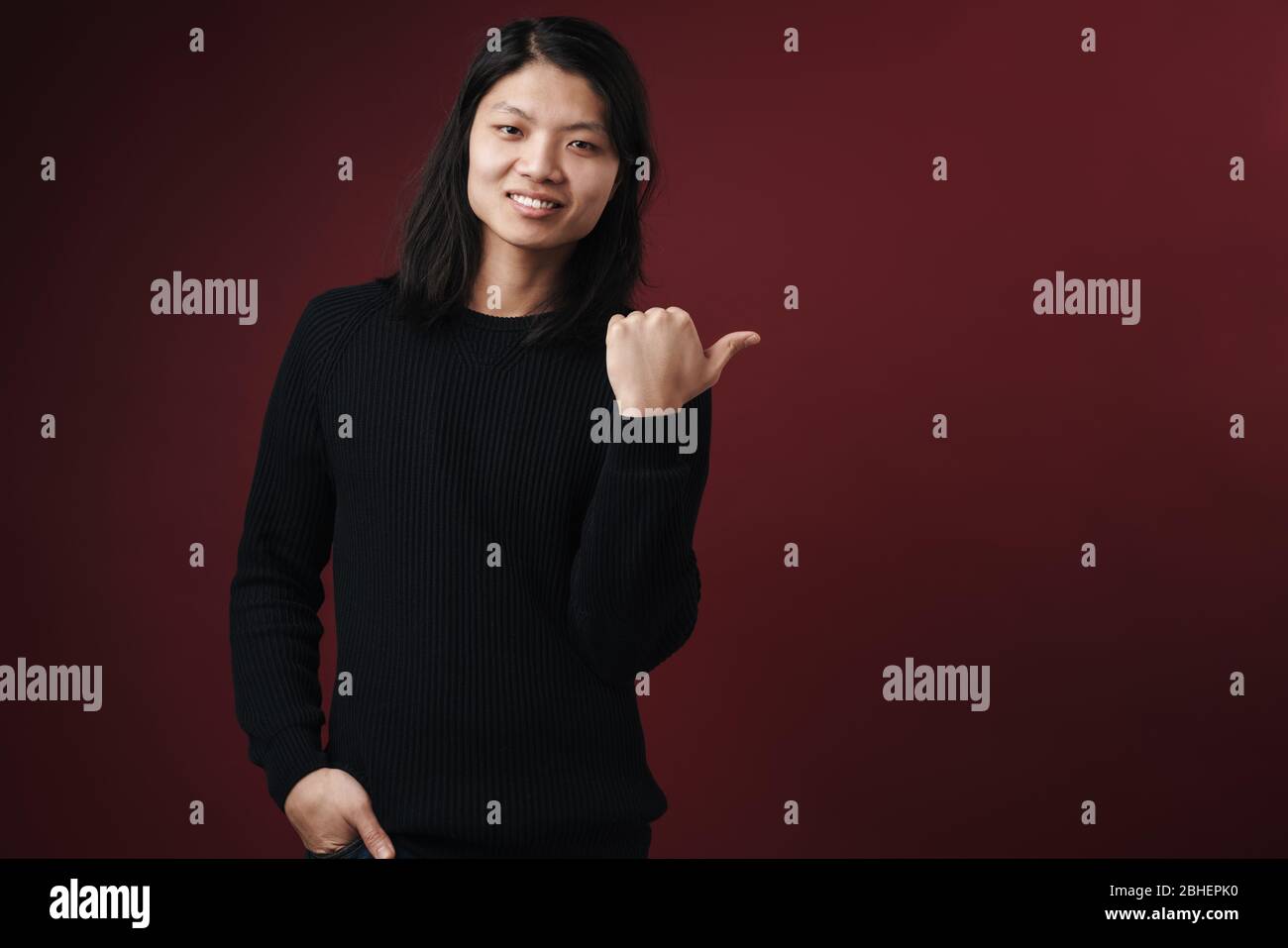 Image of joyful asian man smiling and pointing thumb aside isolated ...