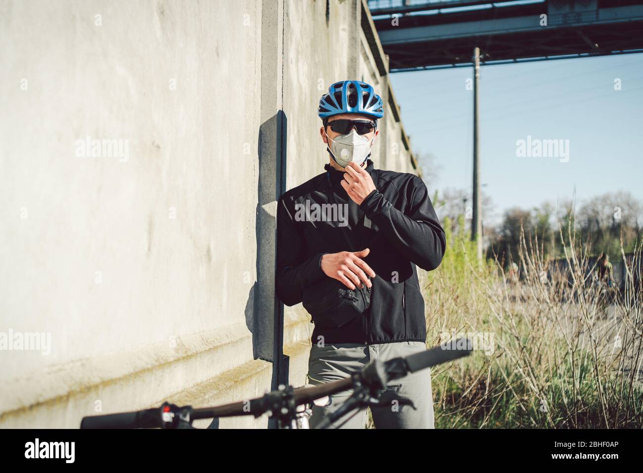 A man cyclist in a protective face mask stands next to a bicycle on a ...