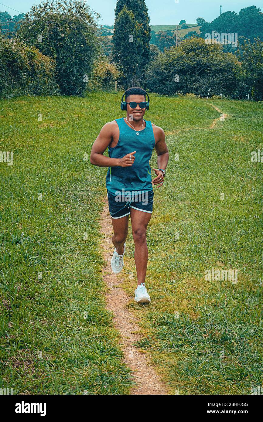 Young fit man with sunglasses smiling while running in the park and ...