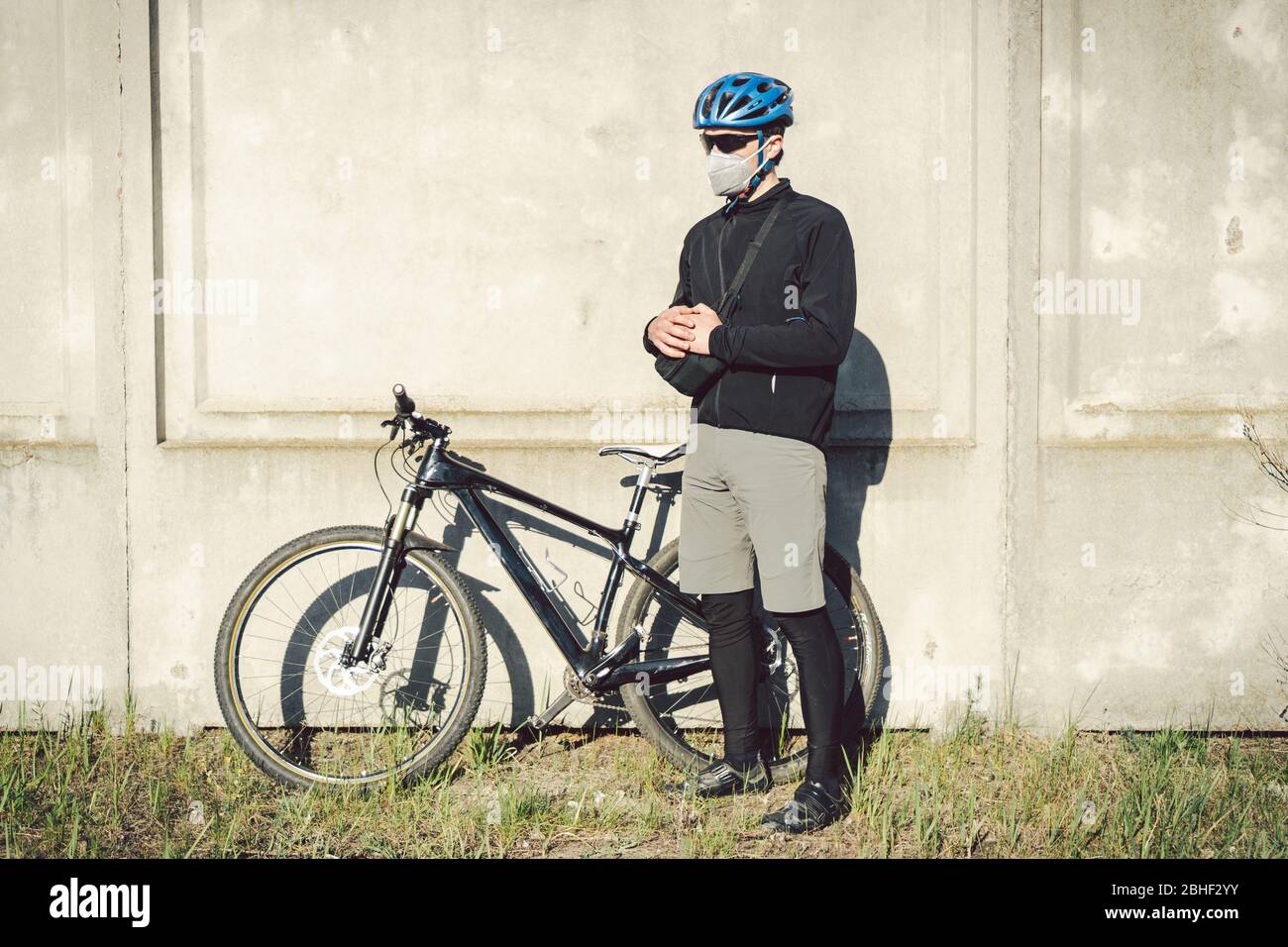 A man cyclist in a protective face mask stands next to a bicycle on a ...