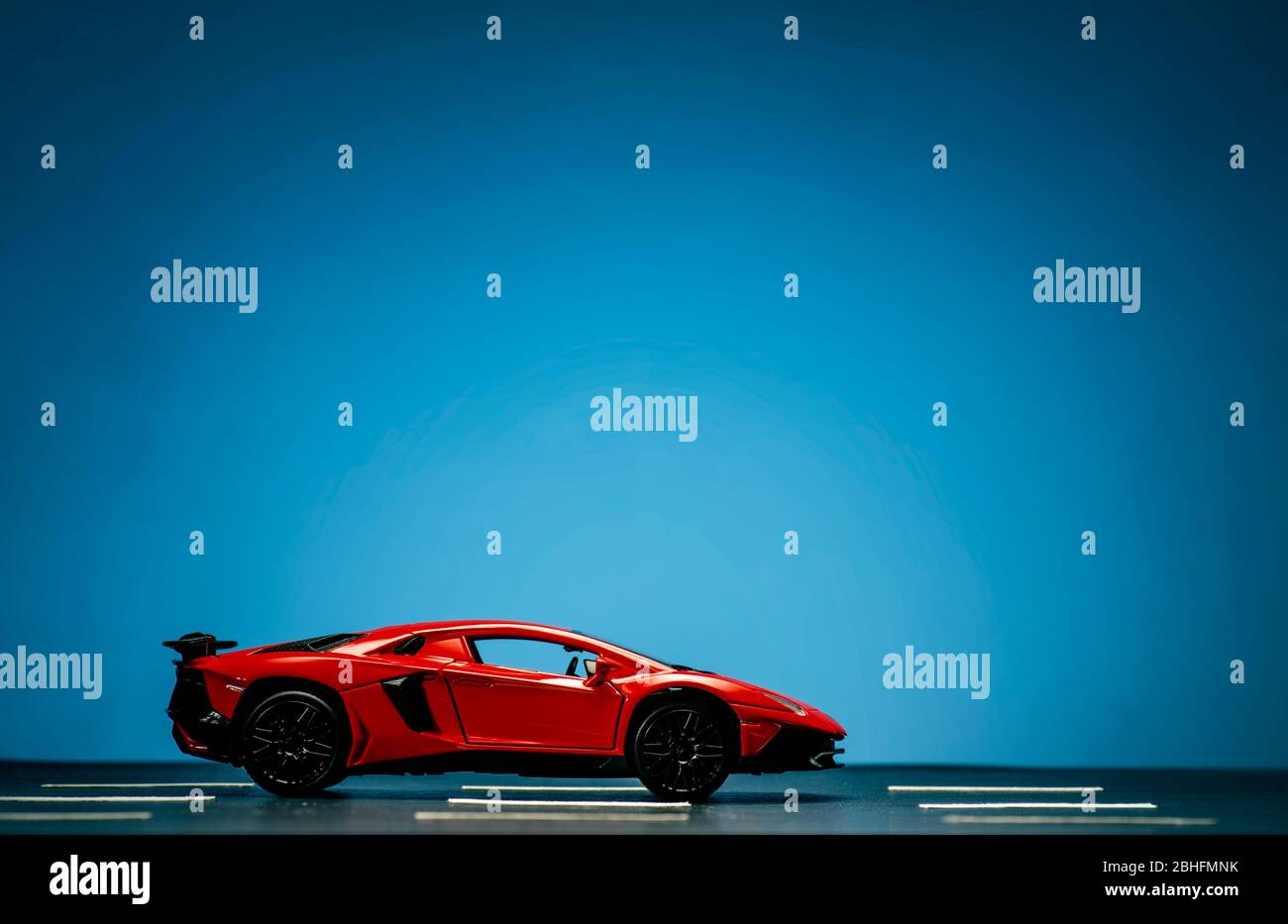 Side view of a red sports car on an asphalt and blue background with ...