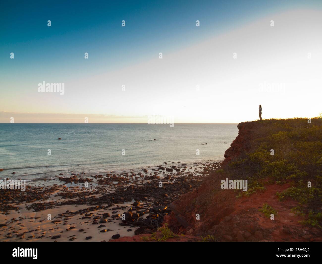 Girl watching sunrise on cliff above Indian Ocean, Pender Bay, Dampier ...
