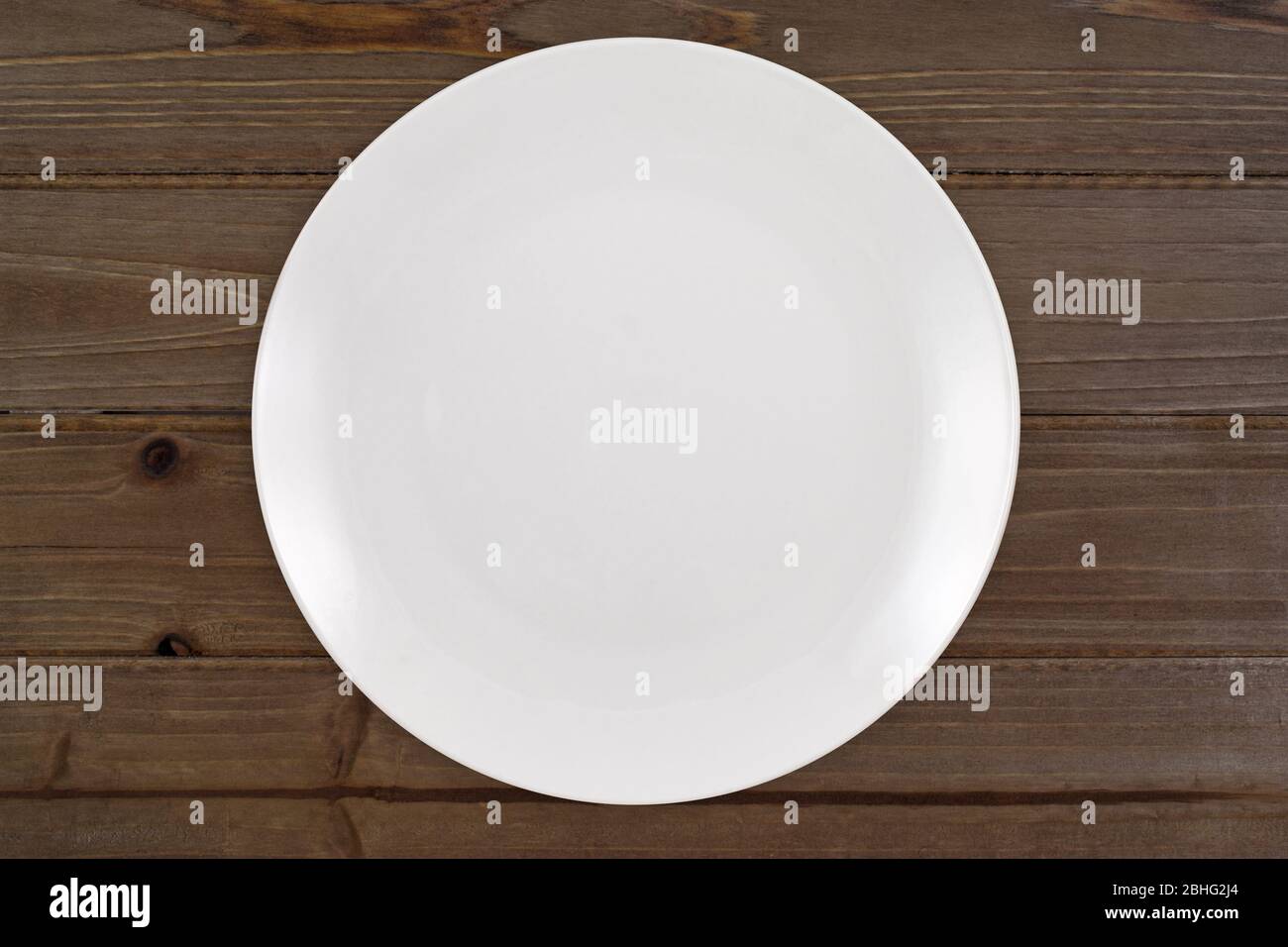 Top down view of a white plate sitting expectantly on a rustic knotted ...