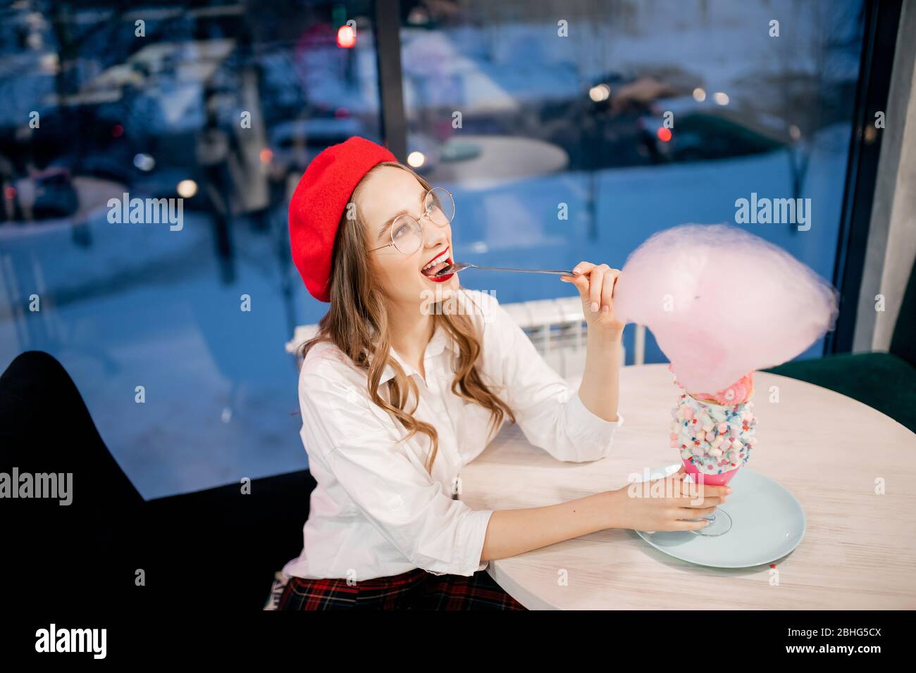 Young woman in red beret and glasses has sweet dessert with candy floss ...