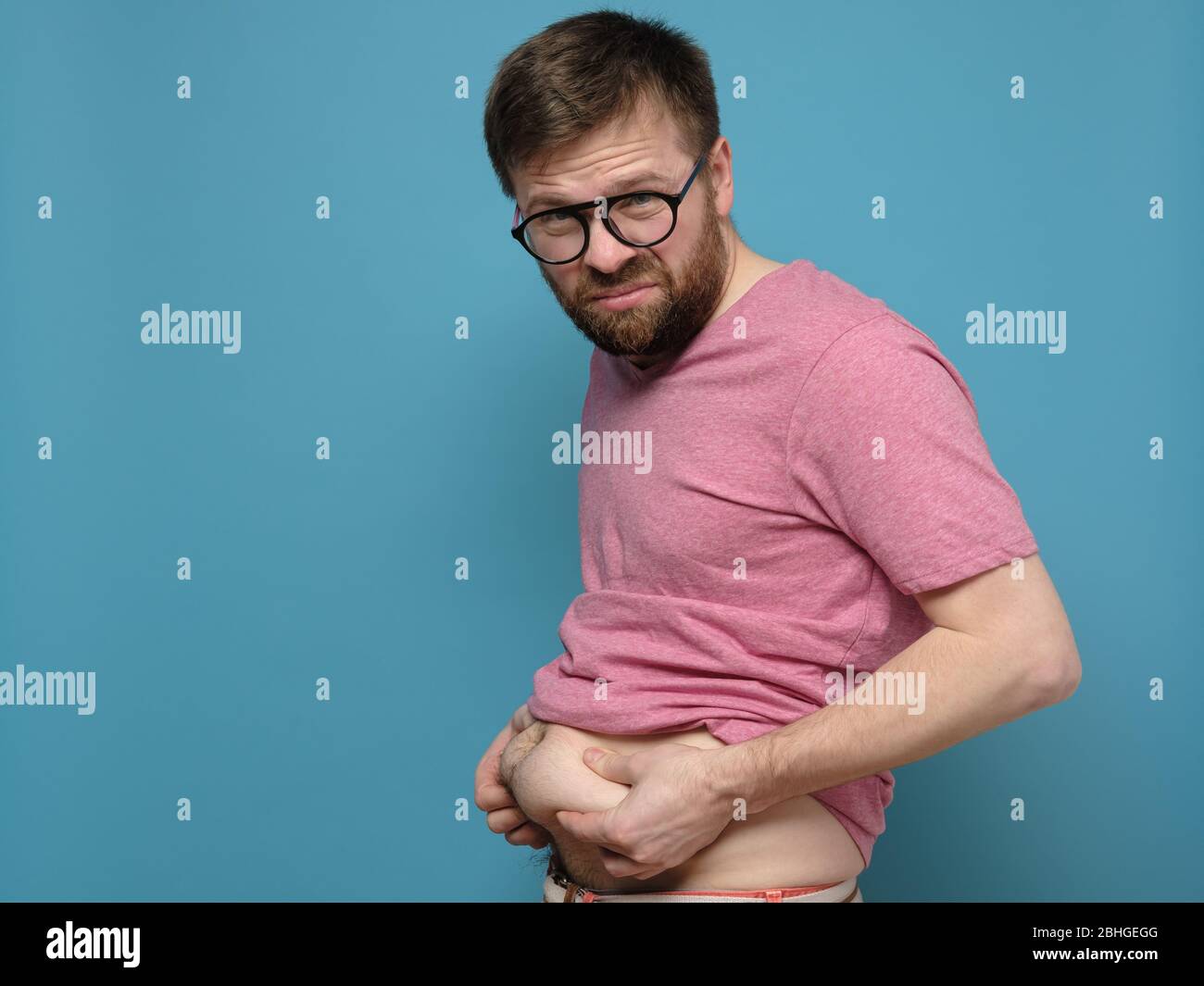 Upset man shows and holds with hands his excess fat on his stomach ...