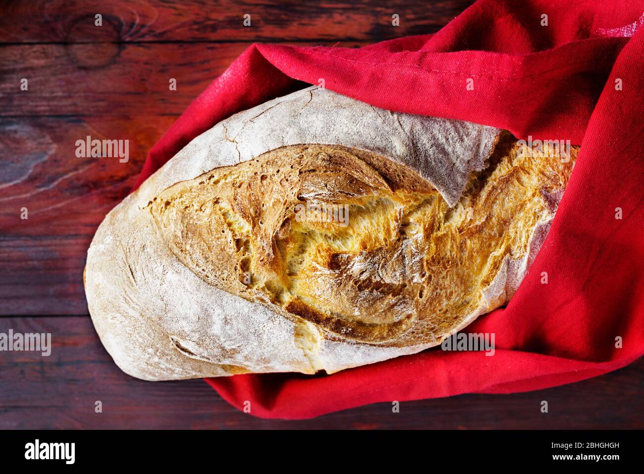 Freshy baked loaf of bread wrapped in red cotton cloth on dark wooden ...